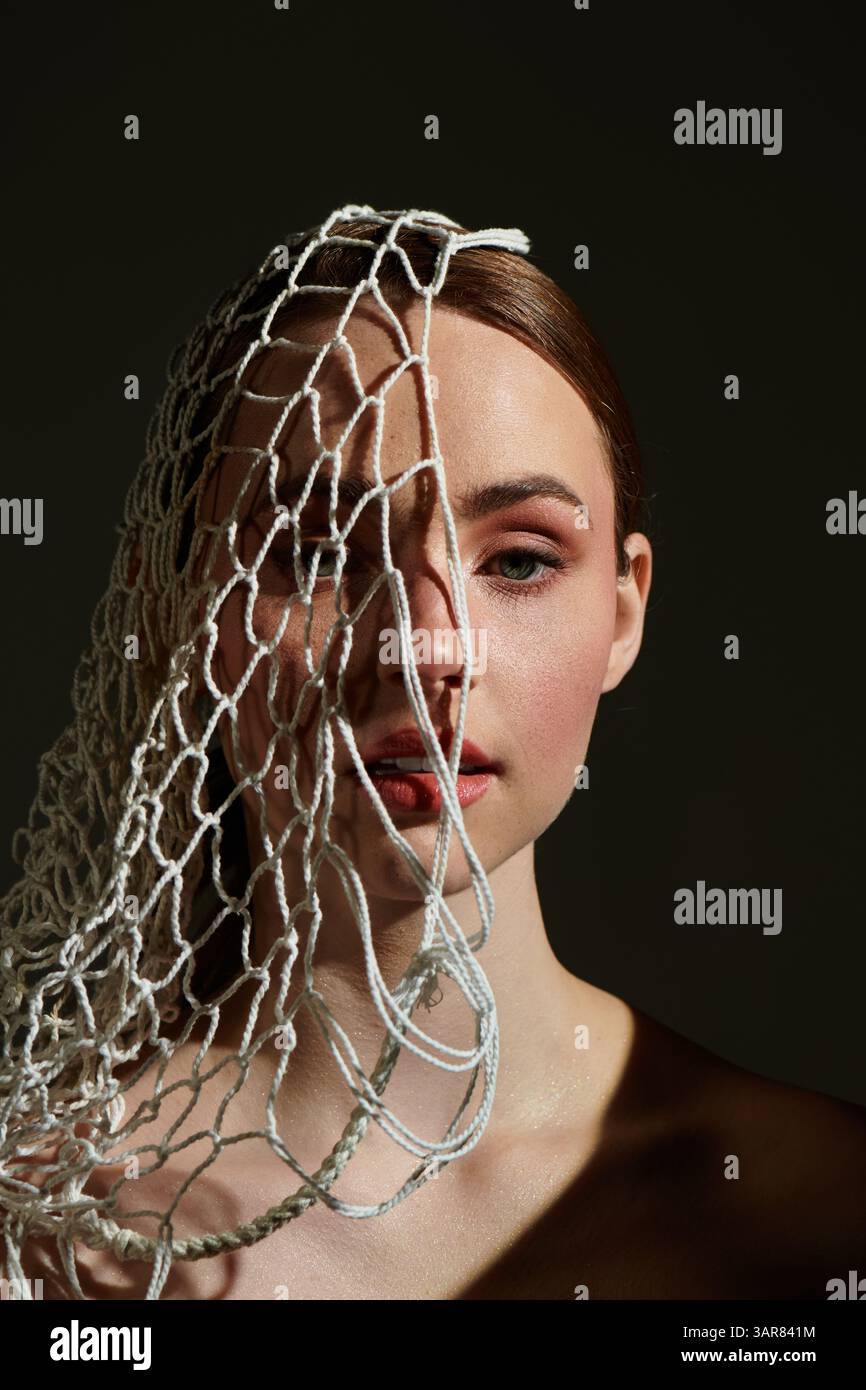 A young woman poses gracefully, her face partly veiled by delicate ...