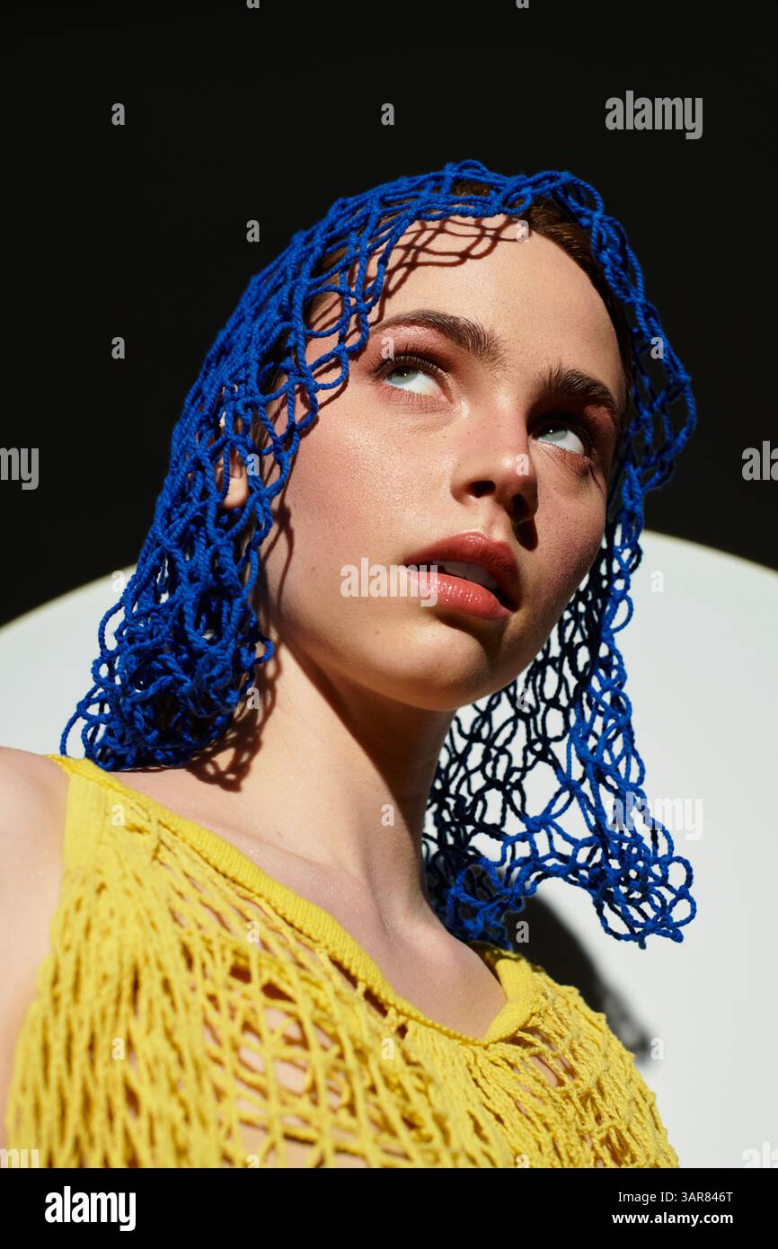 Young woman in a unique blue headpiece stands confidently, radiating ...