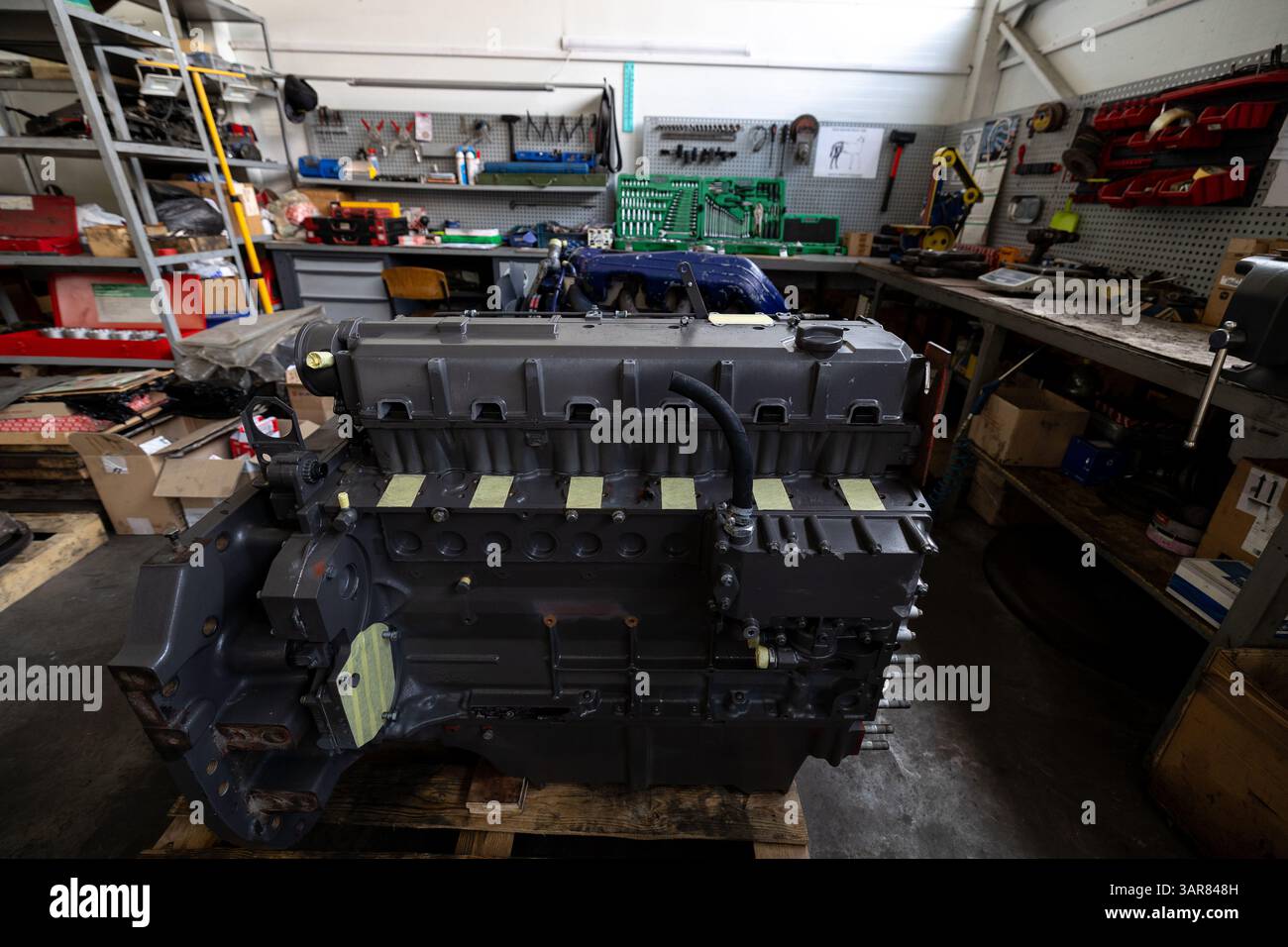 A large, disassembled diesel engine rests on wooden supports in a busy ...