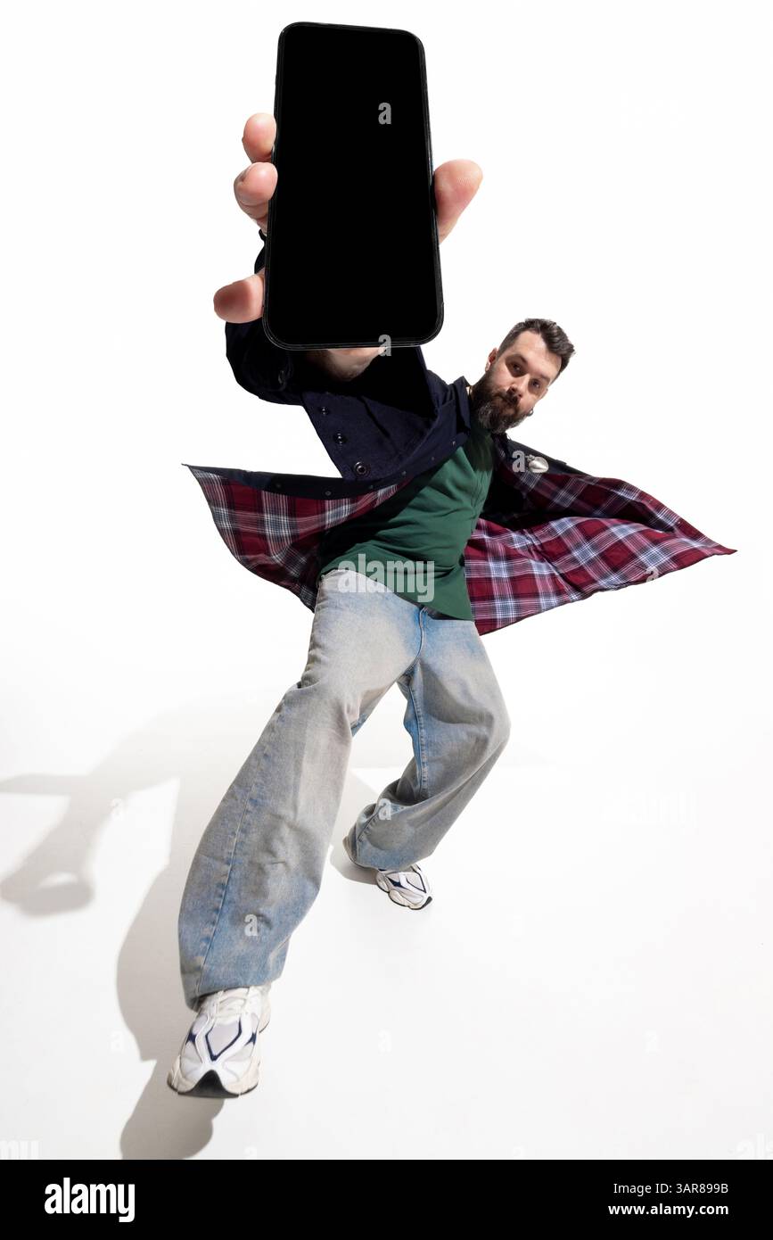 Man in dynamic pose stretches arm forward with smartphone with blank ...