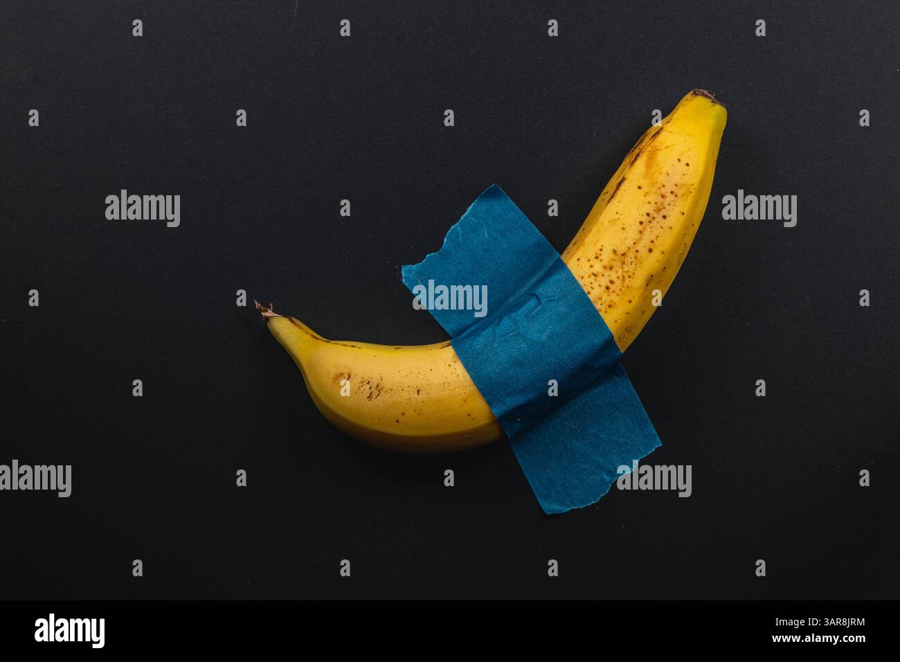 A yellow banana is placed on a black surface with a piece of blue tape ...