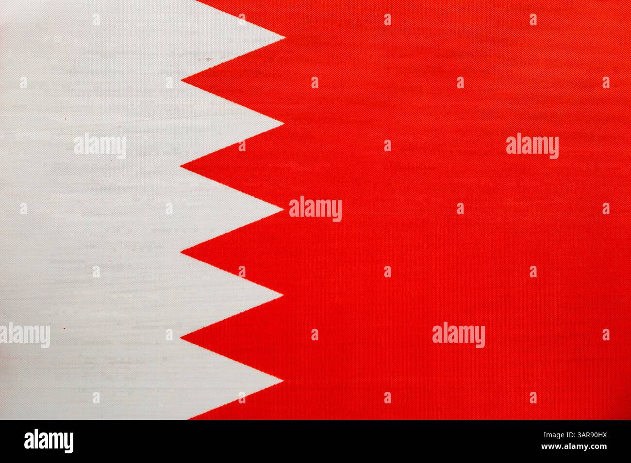 The Bahrain national flag features a red field with a white serrated ...