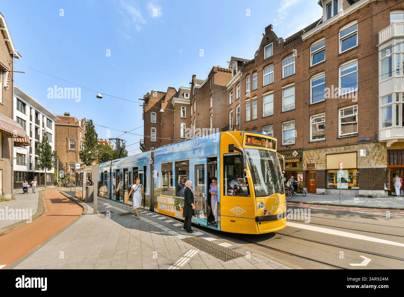 A brightly colored tram stops in a lively city street with pedestrians ...