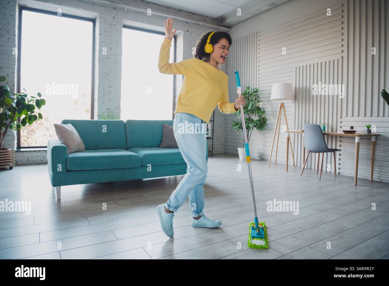 Happy young woman singing and dancing while cleaning her living room ...