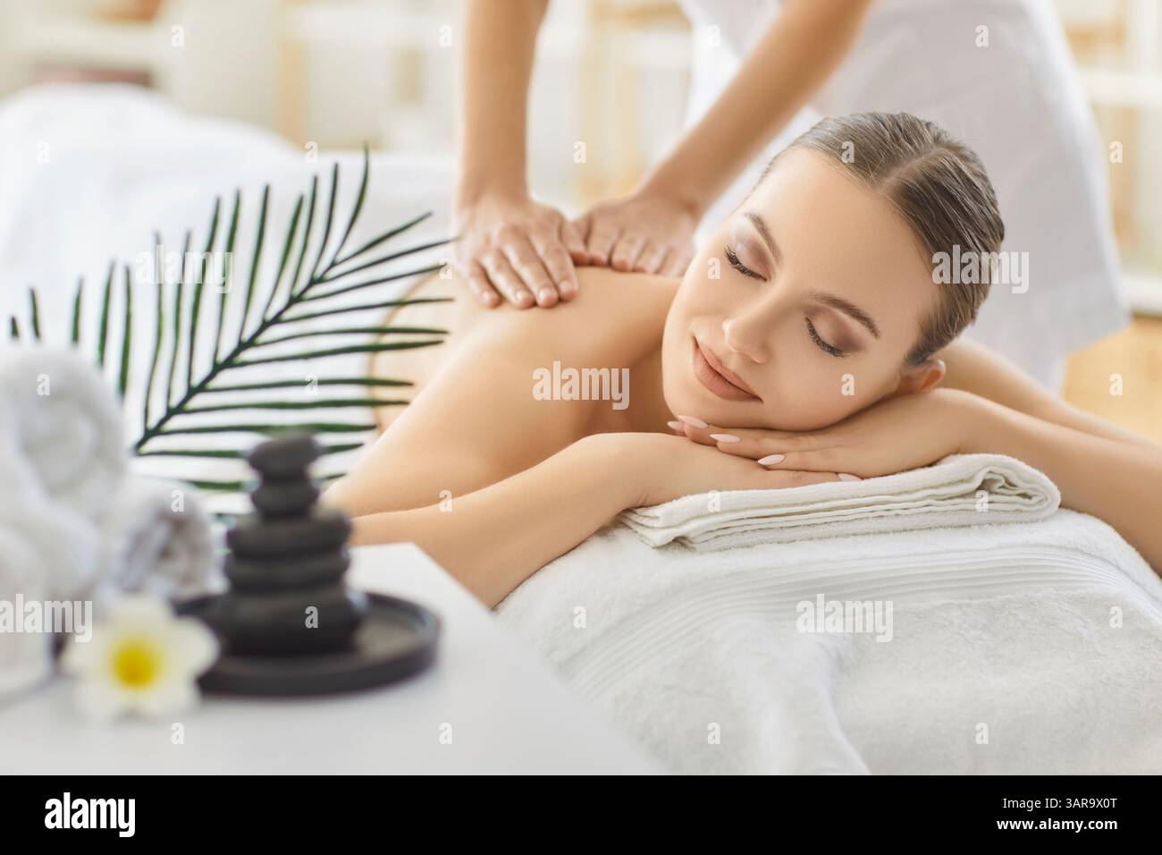 Young woman enjoying spa massage in salon, lying on table with closed ...