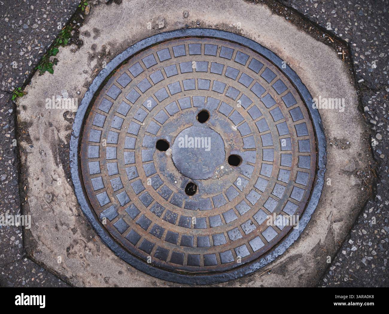 old rusty worn solid iron circular manhole cover set in concrete Stock ...