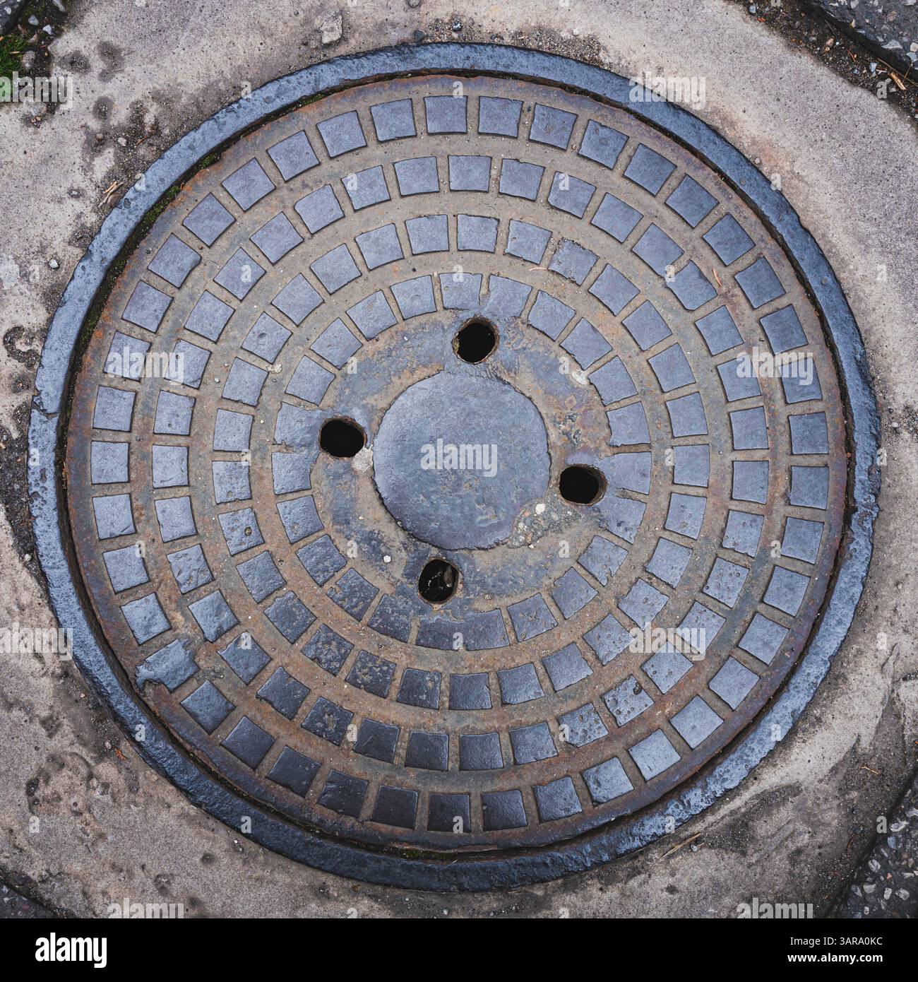 old rusty worn solid iron circular manhole cover set in concrete Stock ...