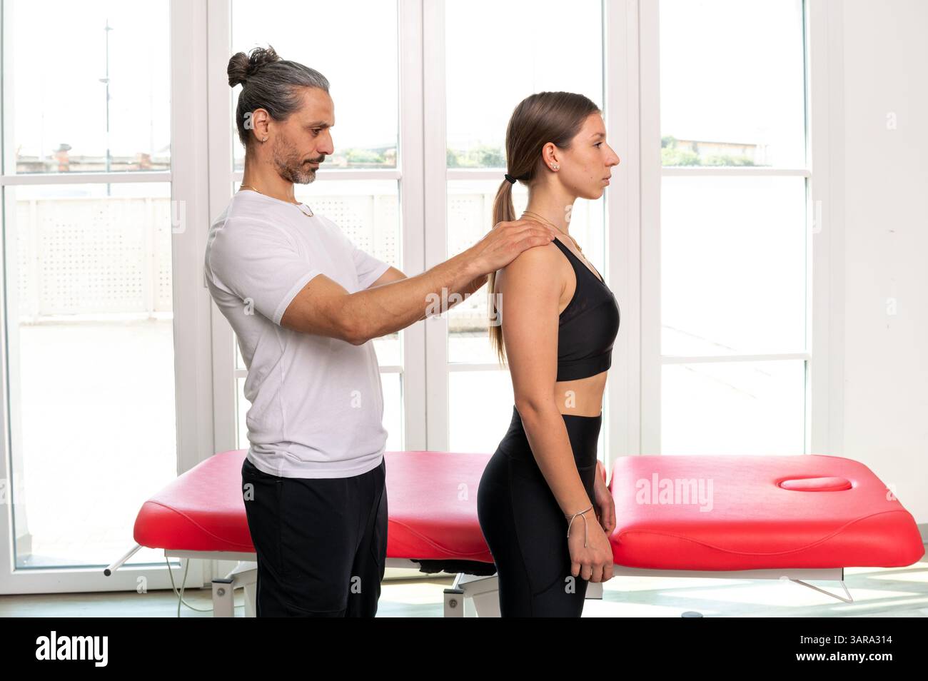 Male osteopath doing a postural evaluation on a young female patient assessing the alignment of ...