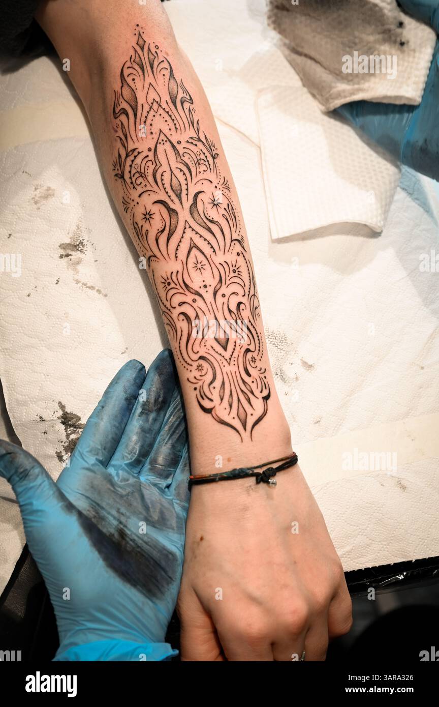 Tattoo artist wearing blue gloves drawing black ink decorative tattoo ...