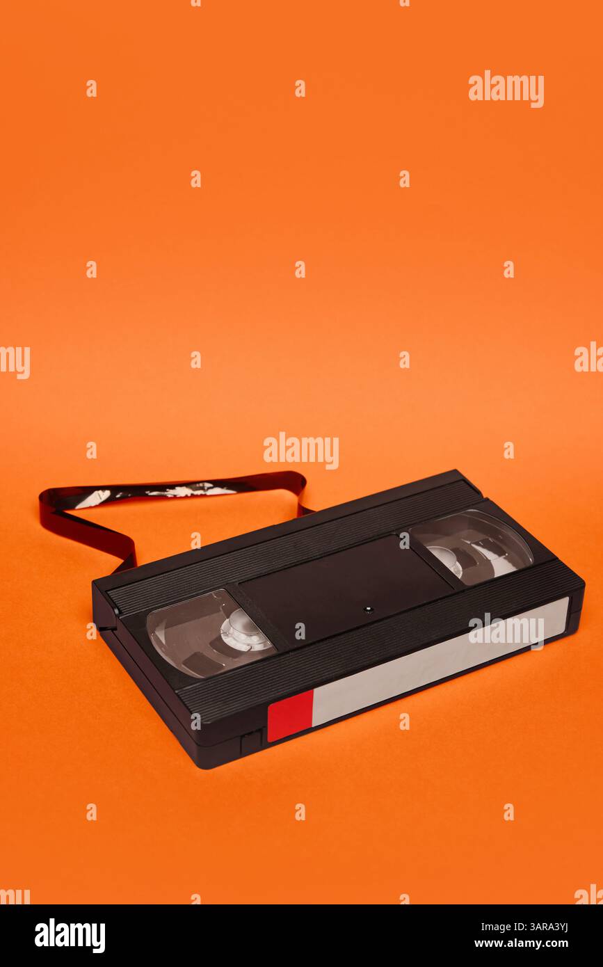 VHS cassette with part of tape unraveled on orange background. Decay of ...