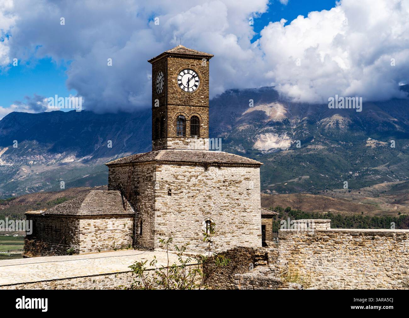 A historic stone clock tower stands against a backdrop of mountains and ...