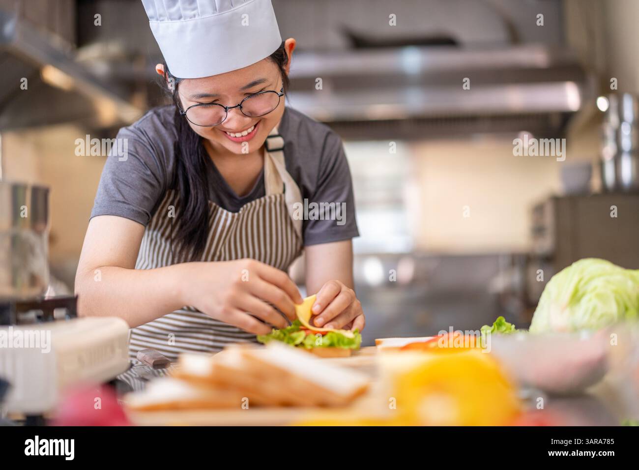 A cheerful young female chef wearing a striped apron and white chef hat ...