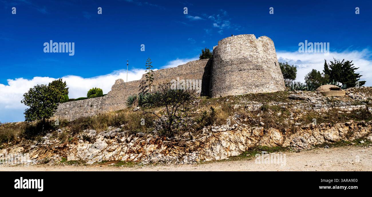 A historic stone fortress on a hillside, surrounded by greenery and ...