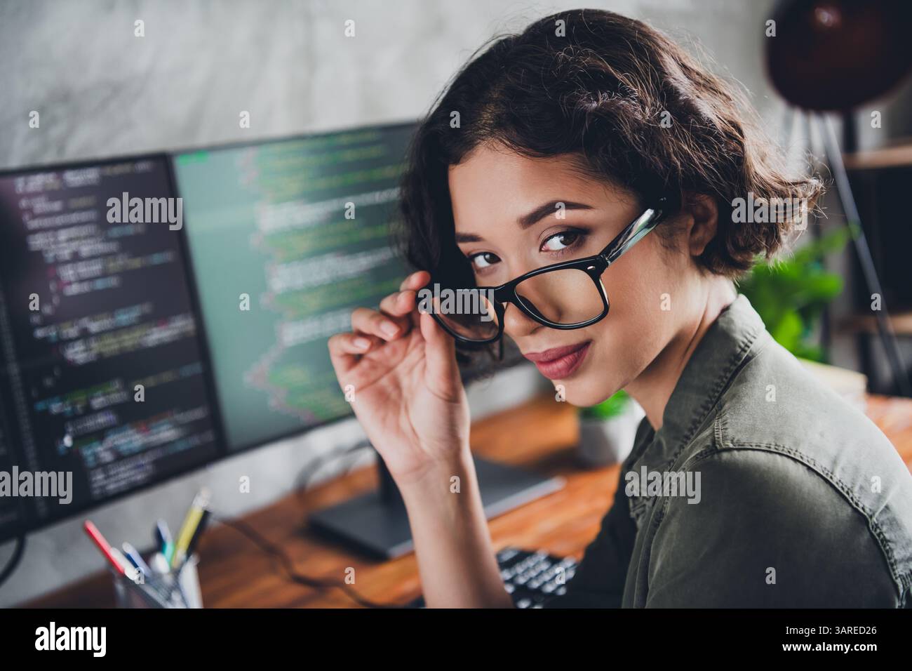 Young professional female programmer with glasses working on code at home office workspace with ...