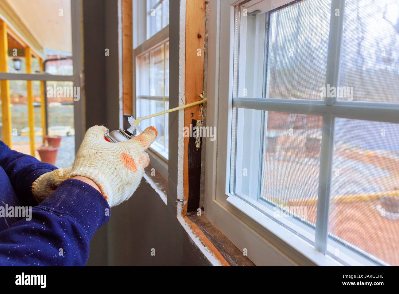 Worker applies sealant foam to window frames, sealing gaps for insulation during home ...