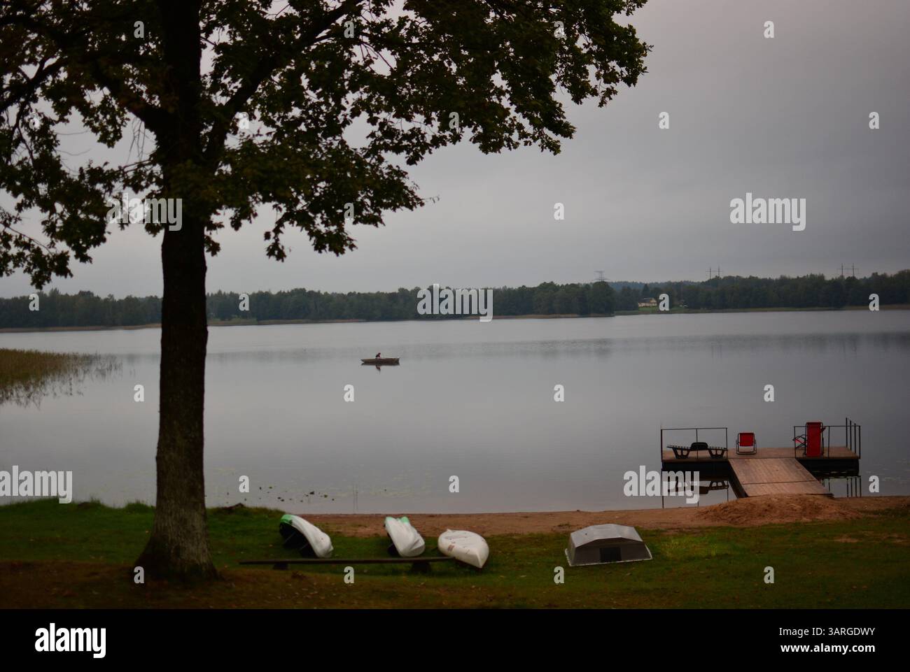 Lake shore with pier, boats and fishing man in boat in the distance ...