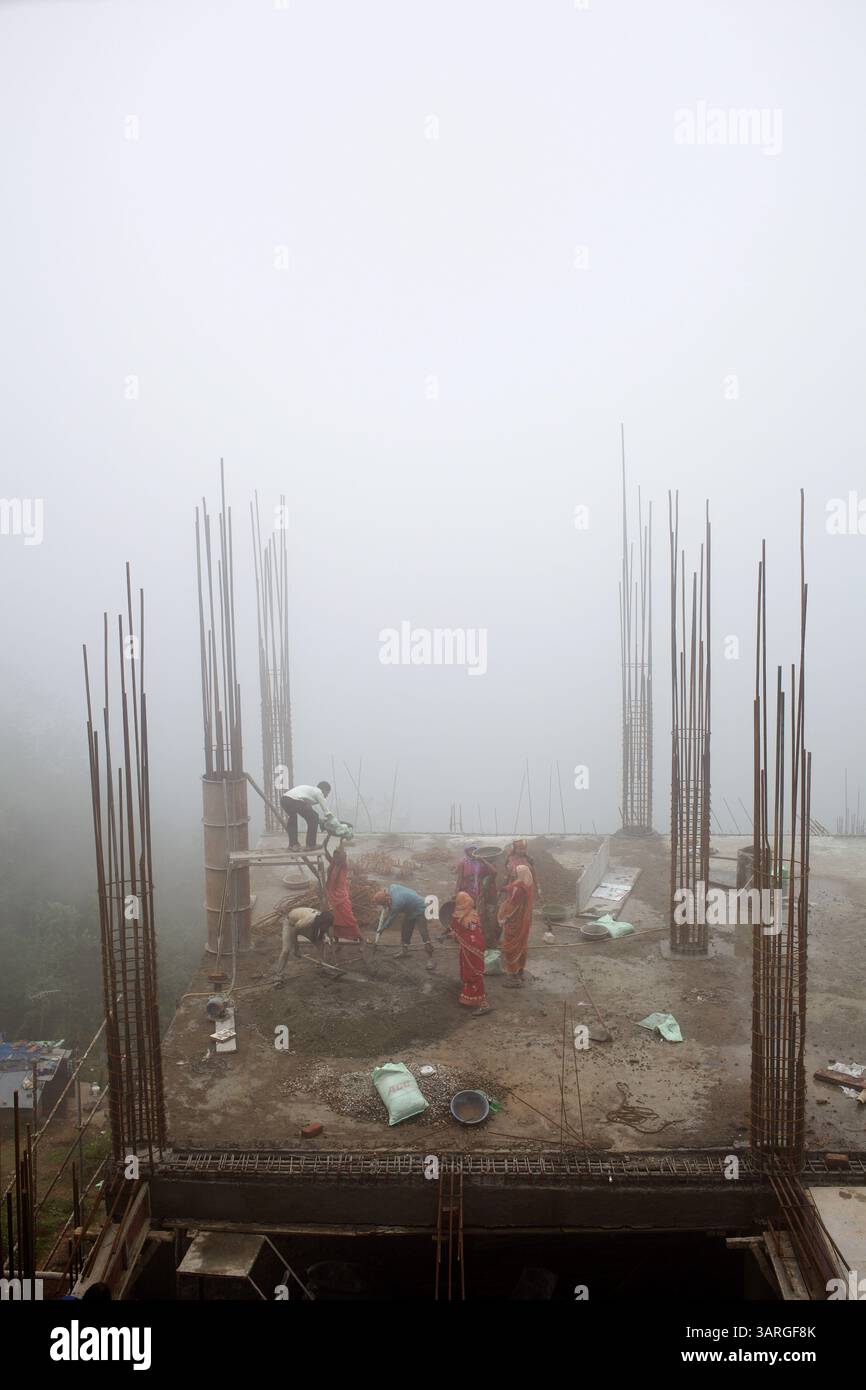 Labourers working on a high-altitude construction site in foggy weather ...