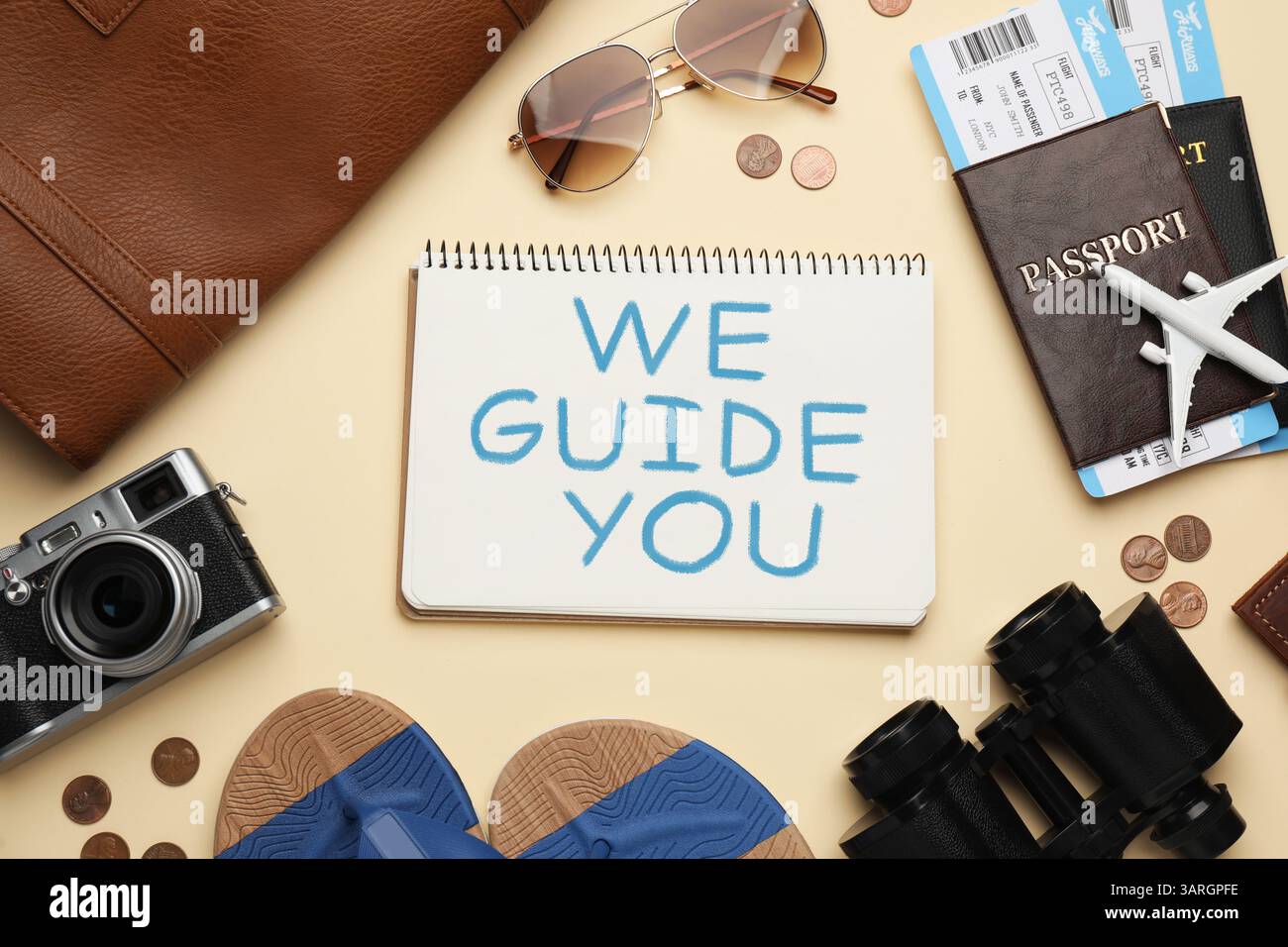 We Guide You text in notebook and different travel items on beige ...
