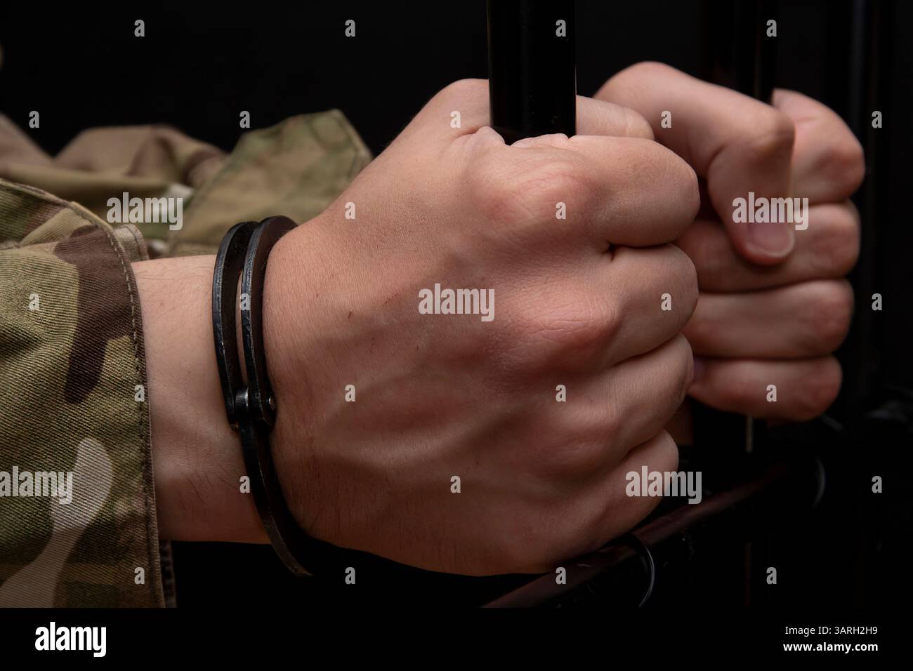 Handcuffed soldier clutching the bars with his hands against a black ...