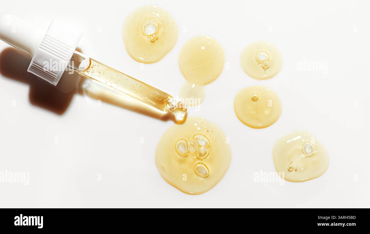 Dropper pipette and drops of golden face serum or retinol gel on white ...