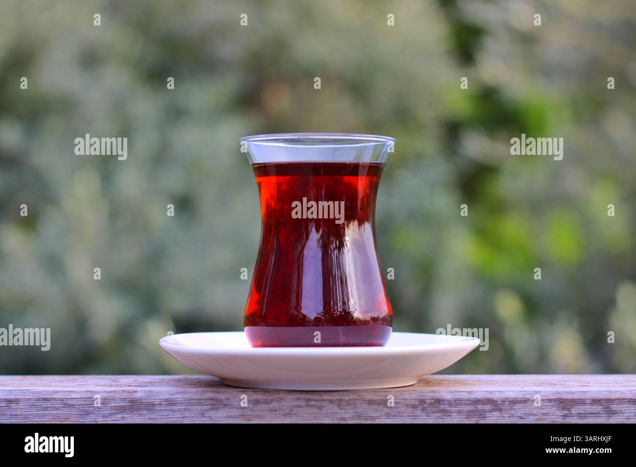 Traditional Turkish tea in a tulip glass on a wooden table with lush ...