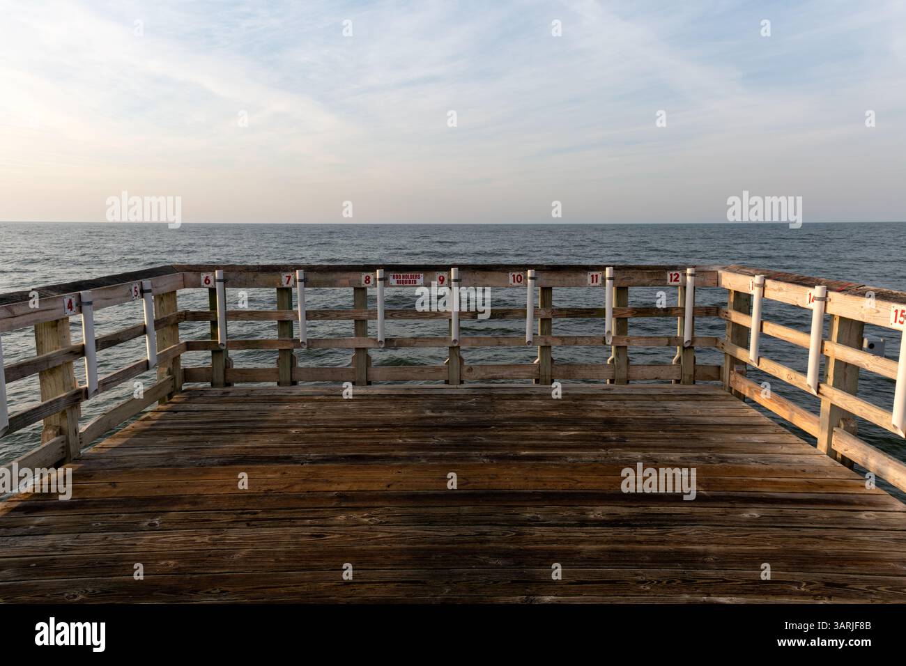 A weathered wooden fishing pier stretches over the ocean under a calm ...