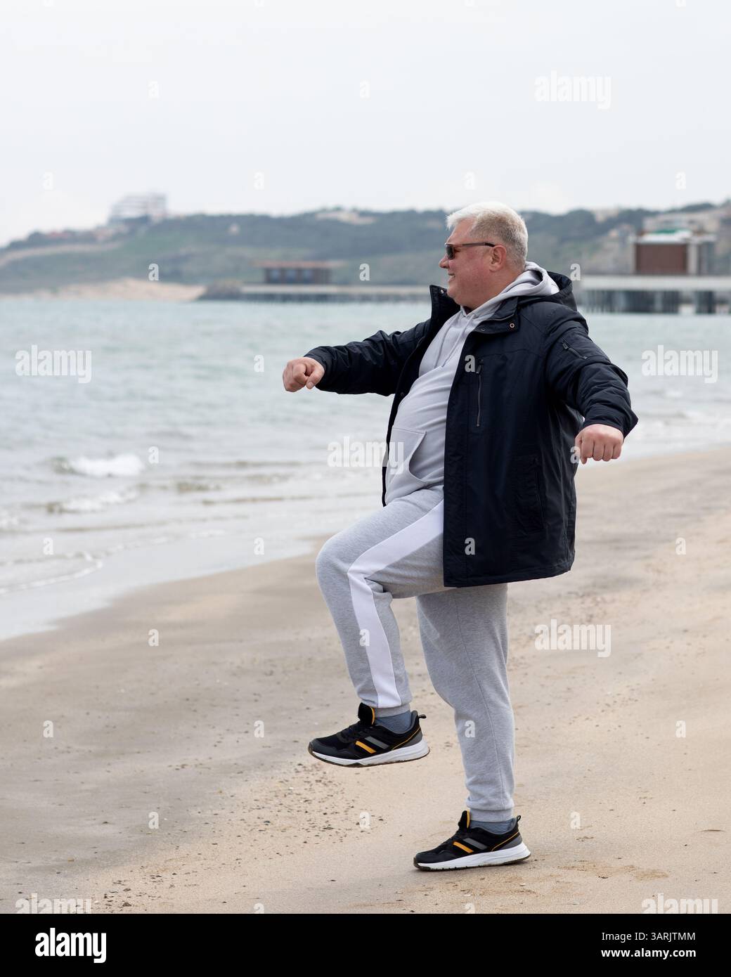 Elderly man enjoying a healthy beach walk on a cloudy day, dressed in ...