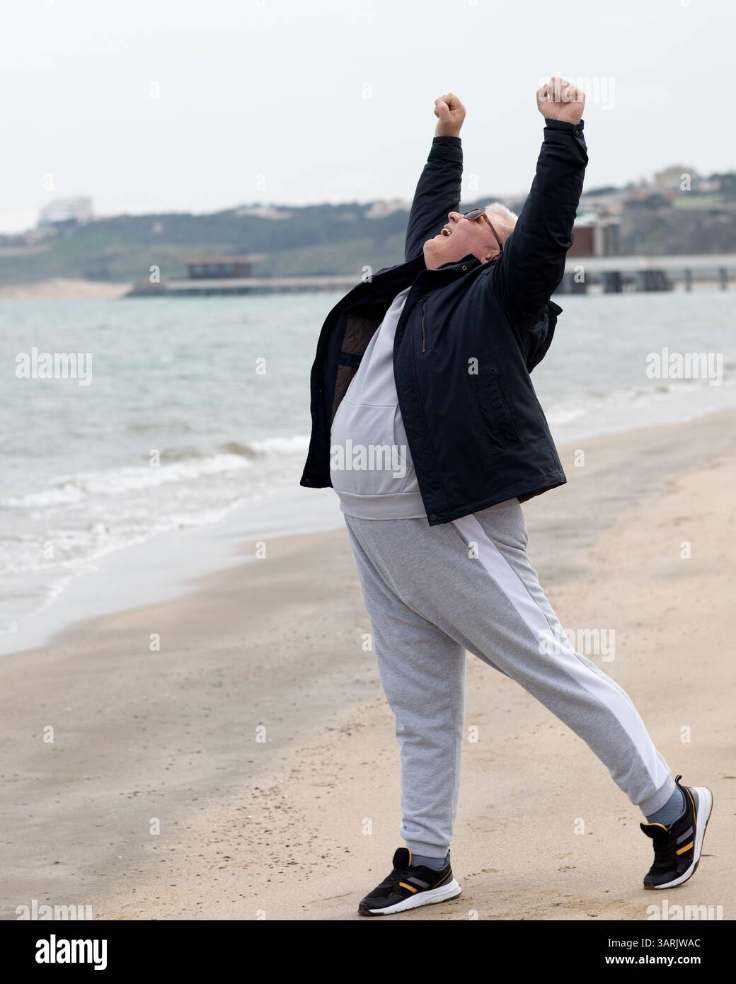 Joyful senior man celebrating life on a chilly beach, wearing a dark ...