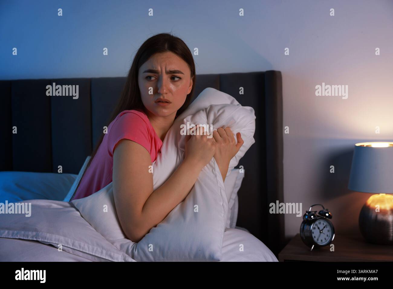Fear of darkness. Scared young woman on bed in room at night Stock ...