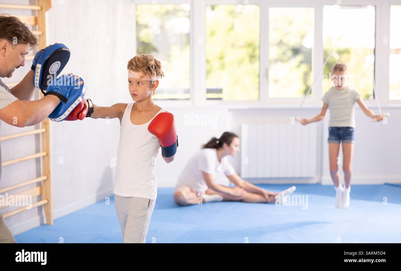 Boy and dad are boxing in gym, father helps child to work out force of ...