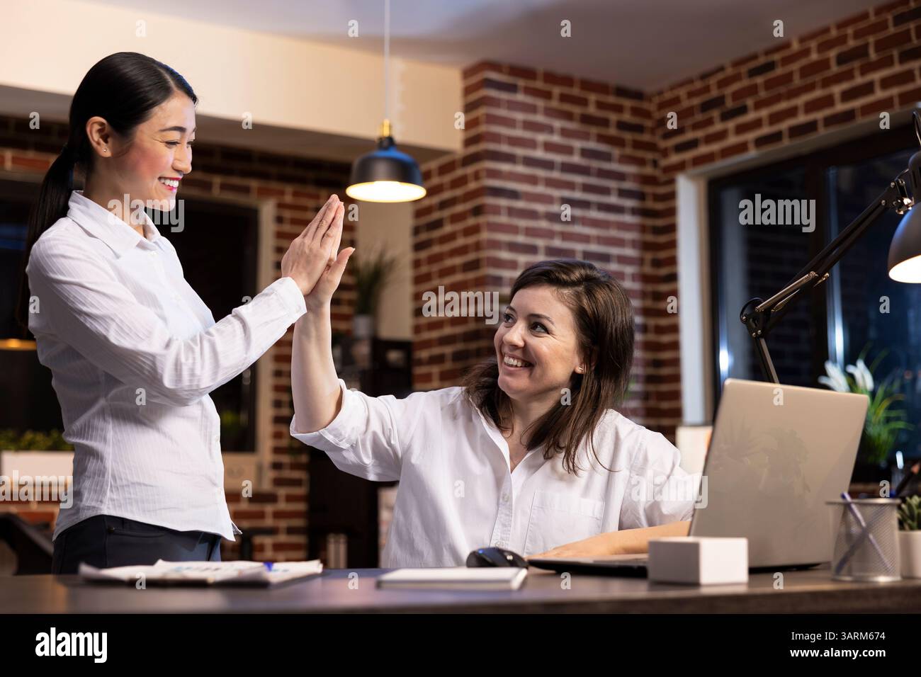 Cheerful professional women in business attire share a high five at an ...
