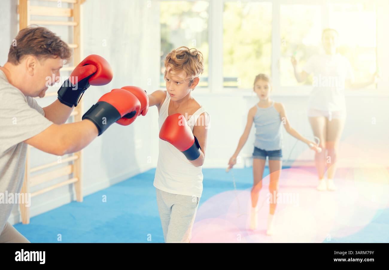 Boy and dad are boxing in gym, father helps child to work out force of ...