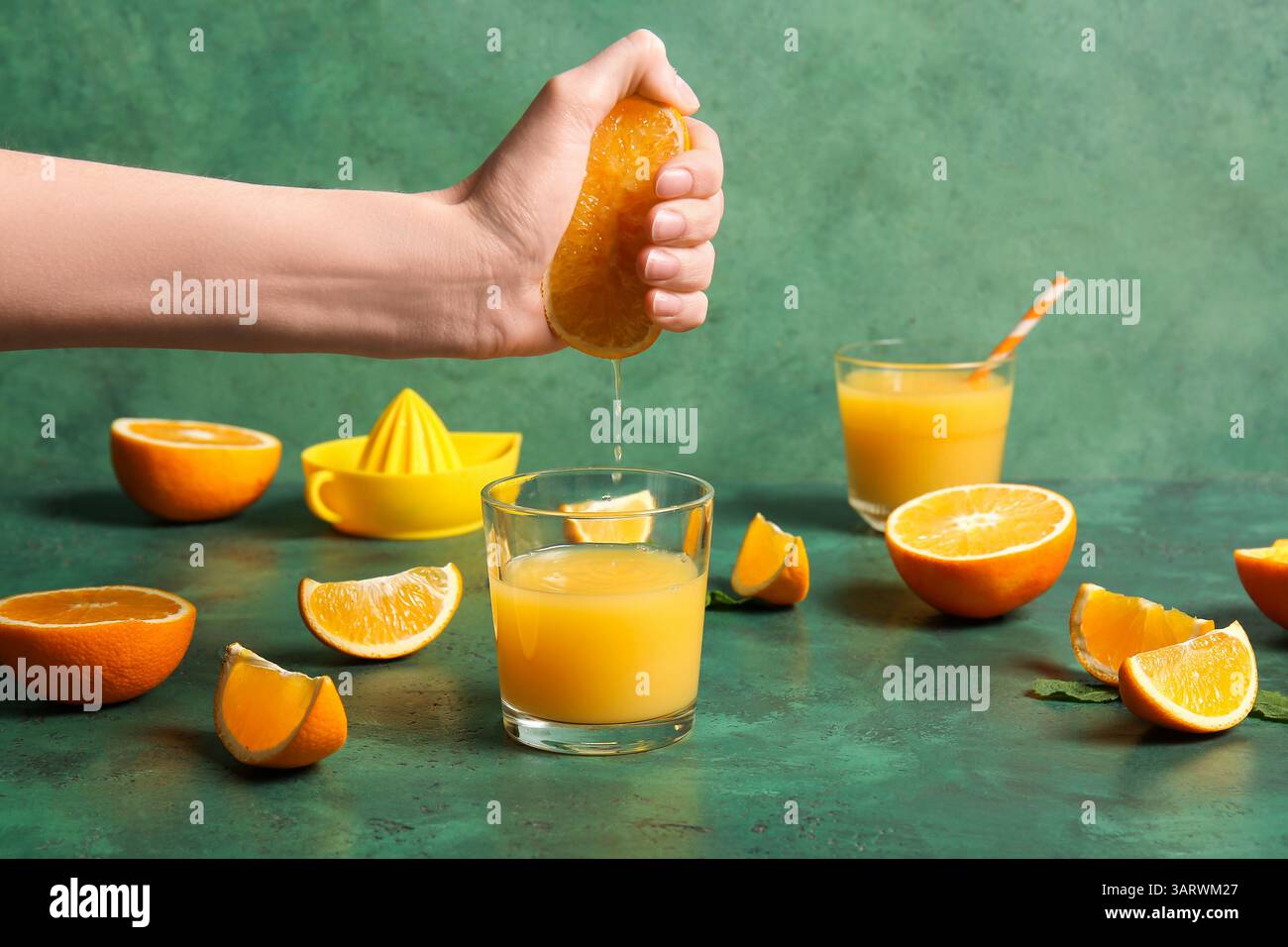 Female hand squeezing orange juice into glass on green background Stock ...