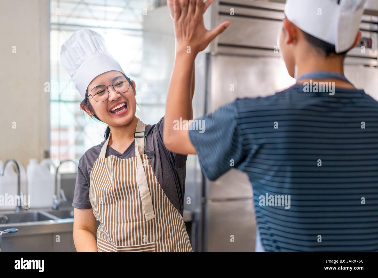 Two young chefs celebrate with a high-five in a commercial kitchen ...
