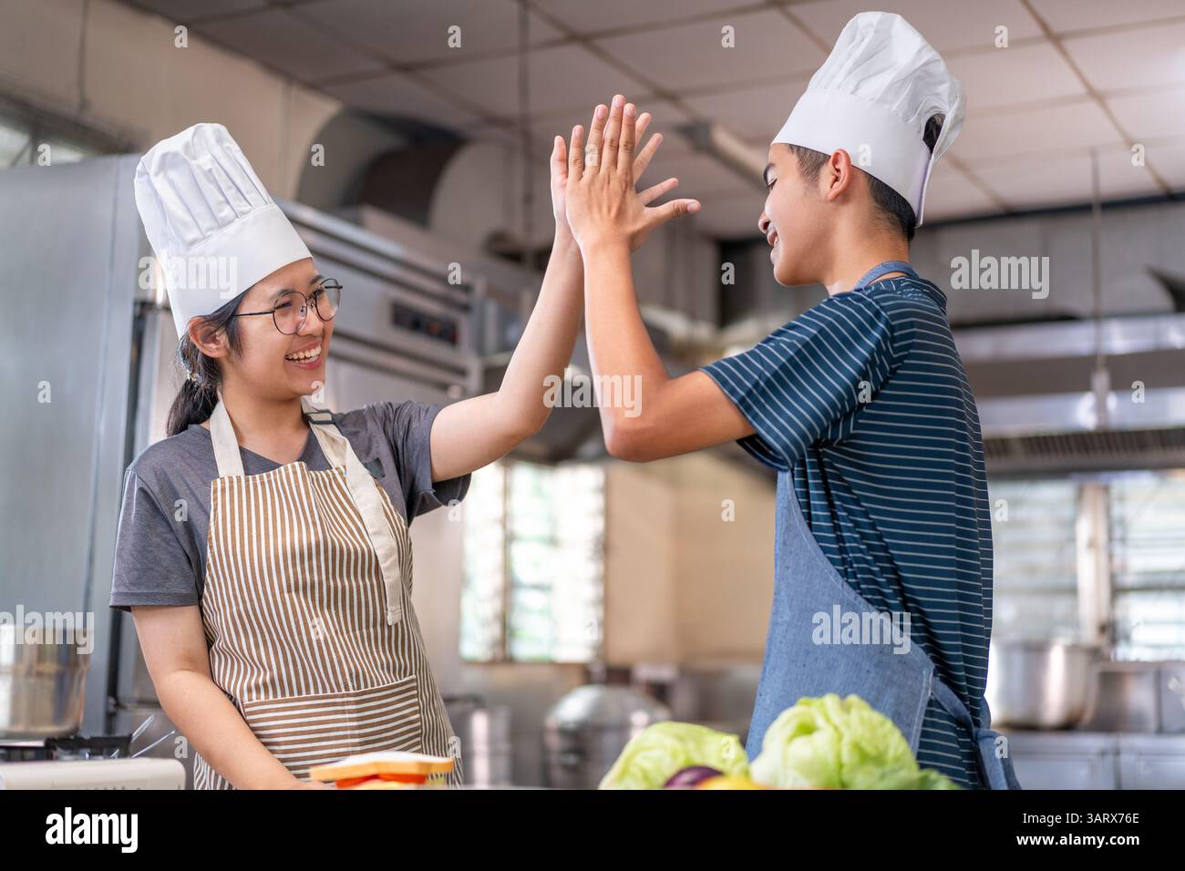 Two young chefs celebrate with a high-five in a commercial kitchen ...