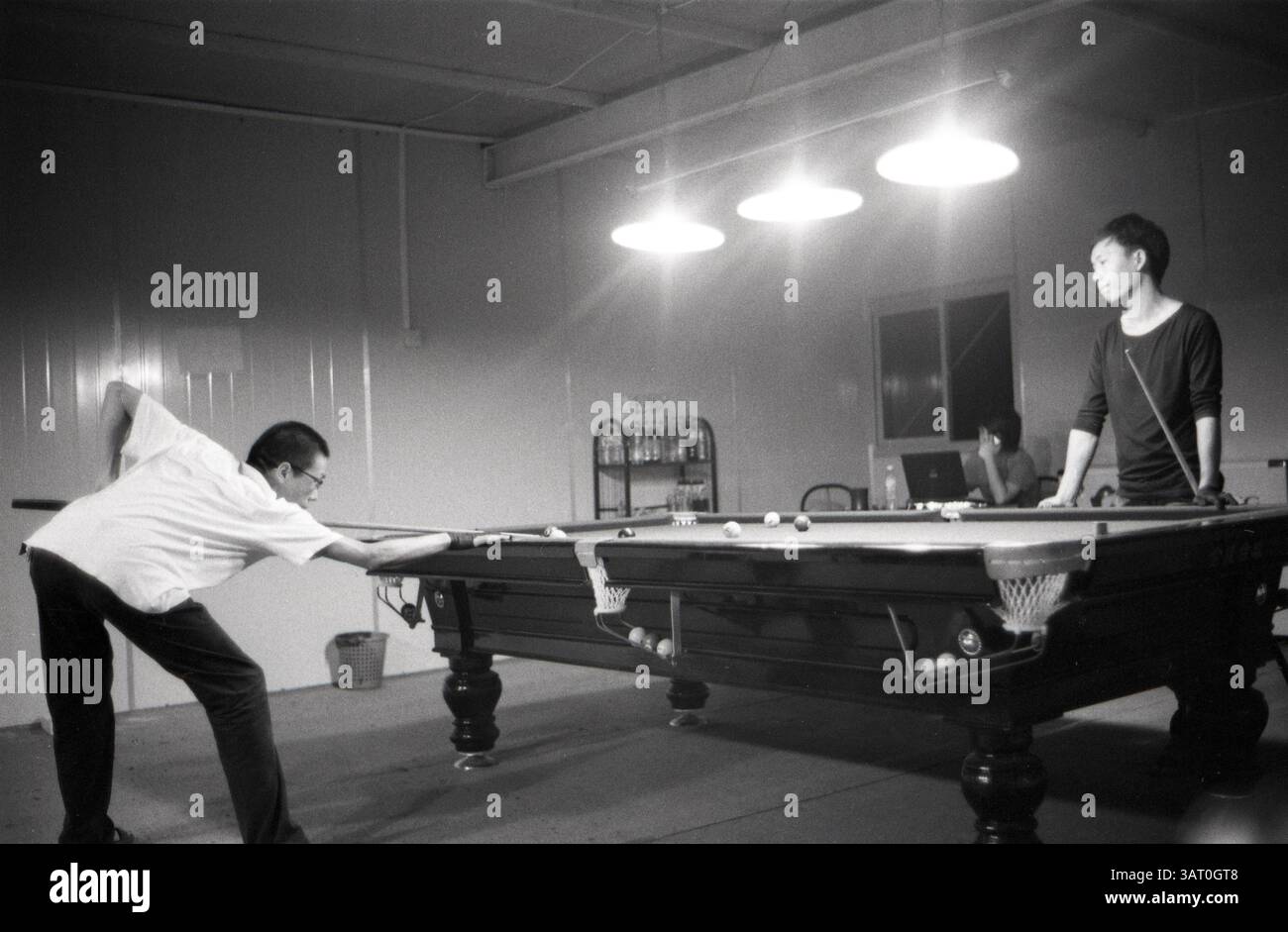 Two players engage in a focused game of billiards in a dimly lit hall ...
