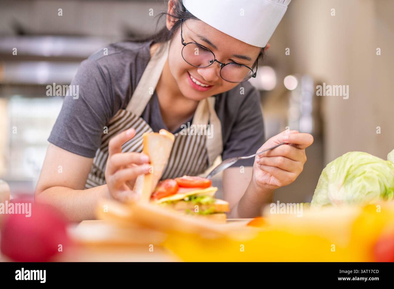A cheerful young female chef wearing a striped apron and white chef hat ...