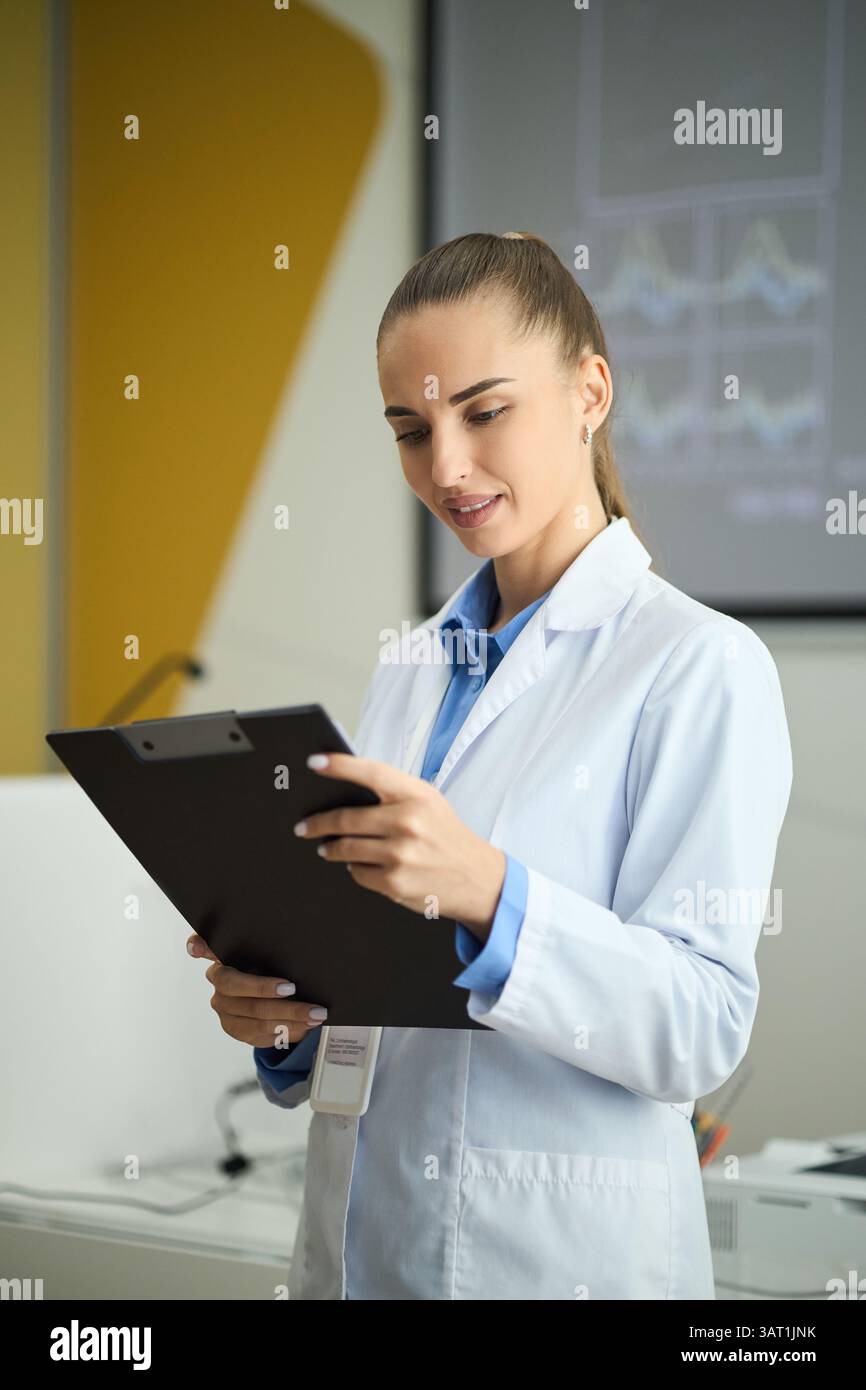Medical professional in lab coat reading from clipboard, standing in ...