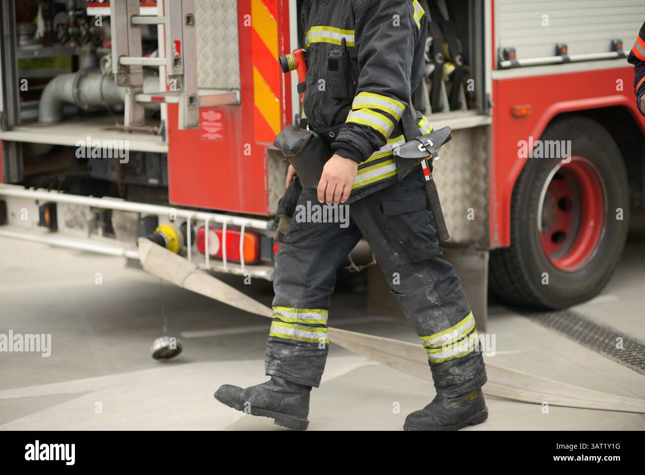 A firefighter in full turnout gear walks beside an active fire truck ...