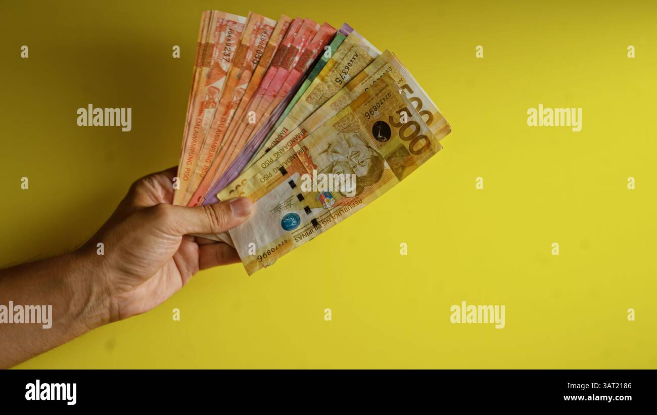 Hand holding various denominations of philippine pesos against a yellow ...