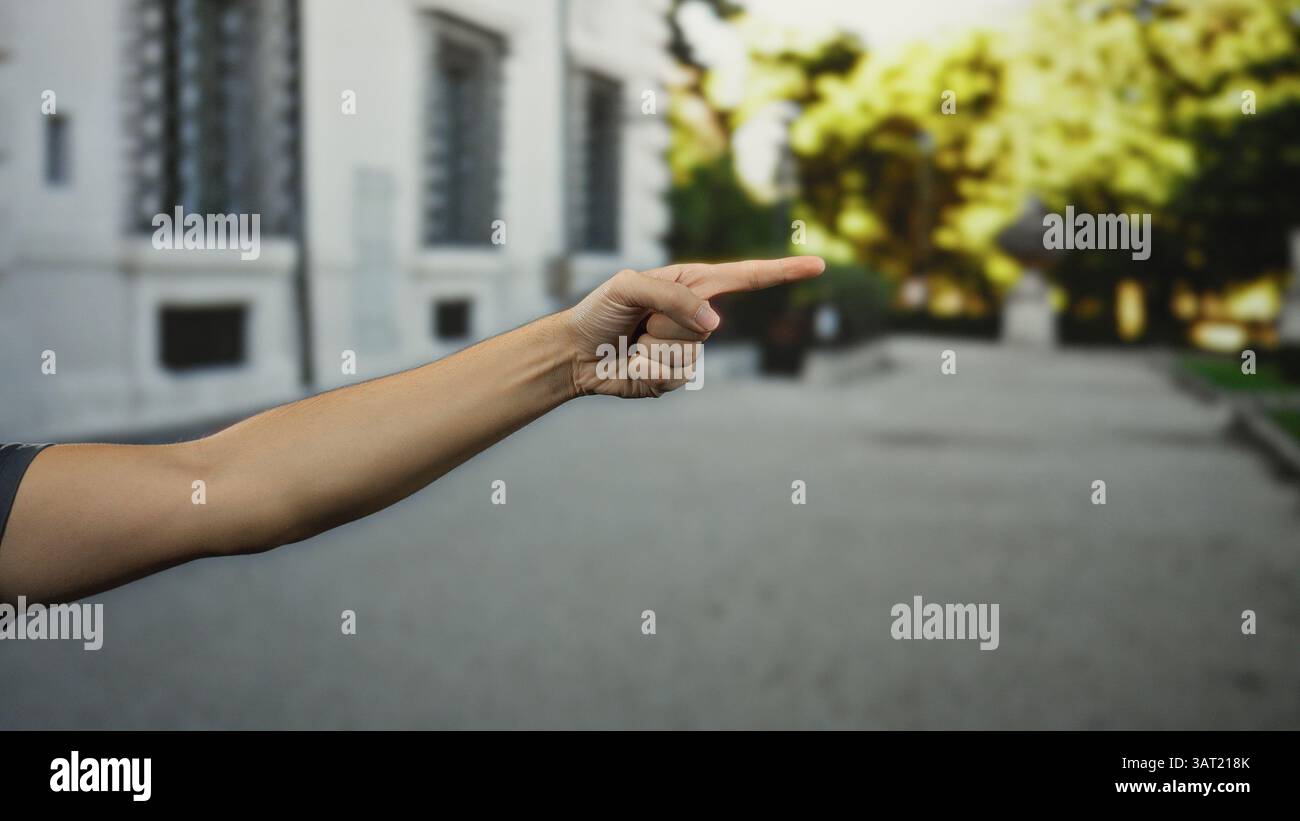 Man's hand pointing on a city street, set against an outdoor urban ...