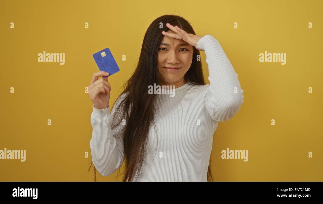 Woman smiling on a yellow background holding a blue credit card ...