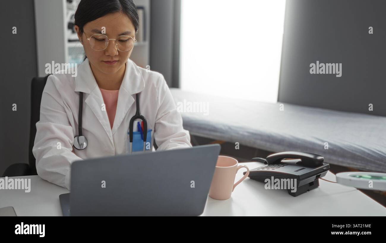 Female doctor in clinic focused on laptop tasks with stethoscope; woman ...