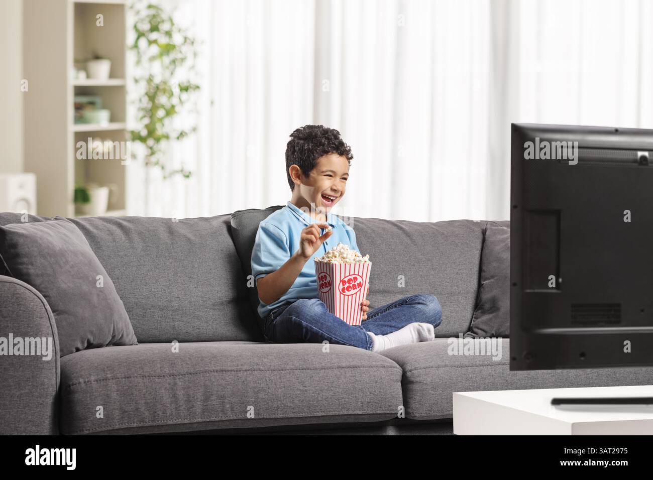 Boy sitting on a sofa eating popcorn and watching tv Stock Photo - Alamy