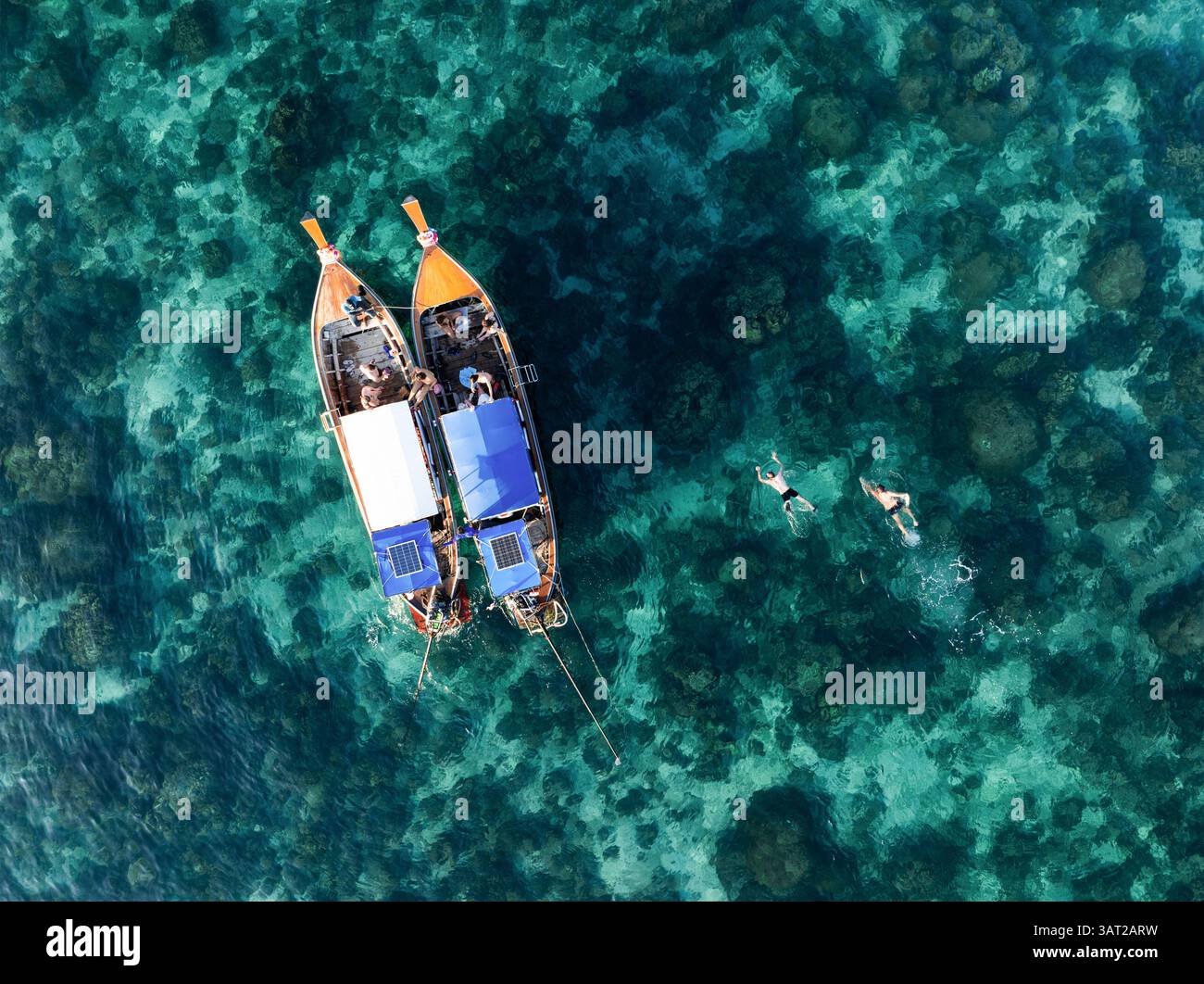 Two traditional boats anchored over a coral reef as people snorkel in ...