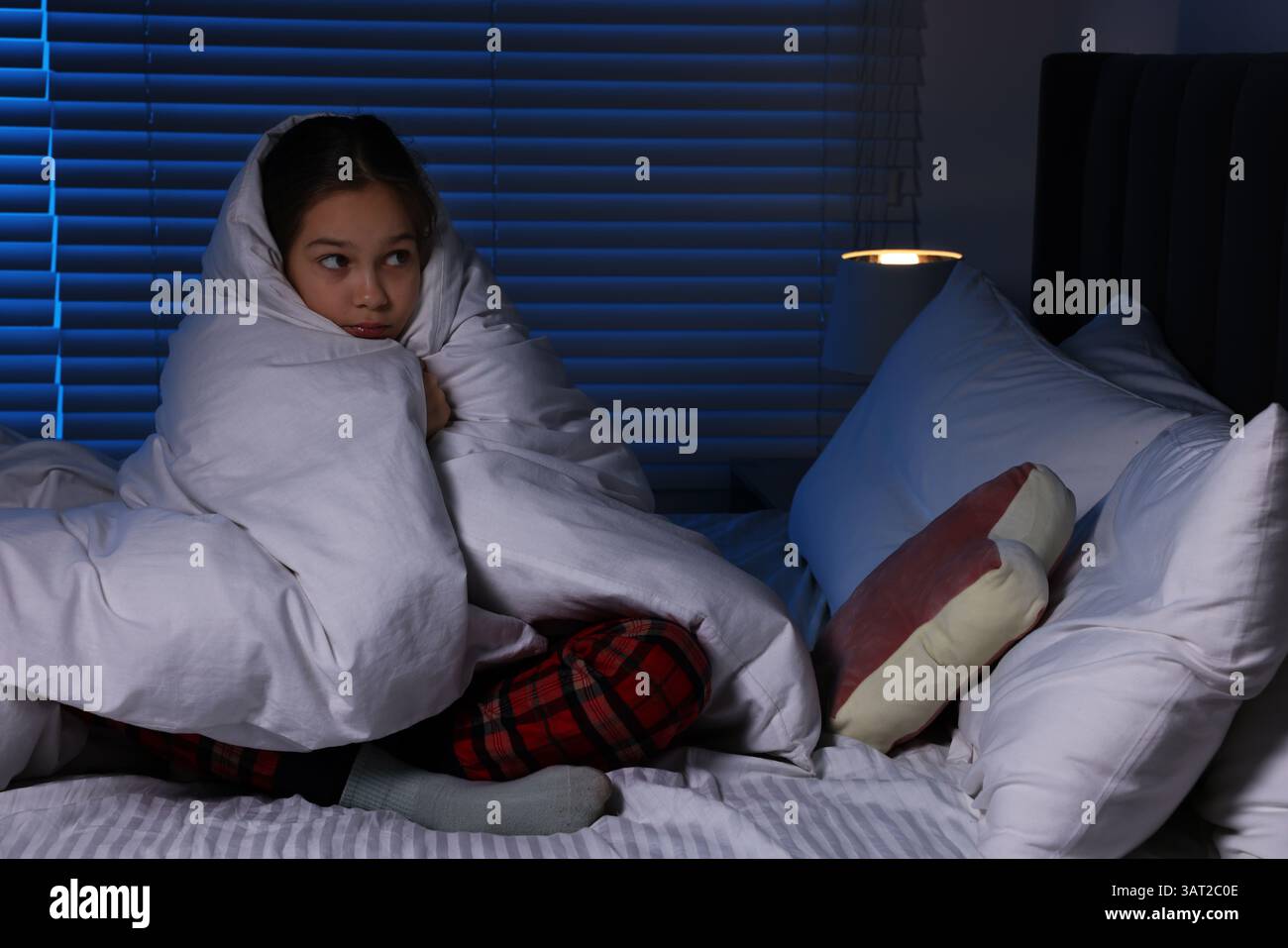 Afraid girl wrapped in duvet on bed at night Stock Photo - Alamy