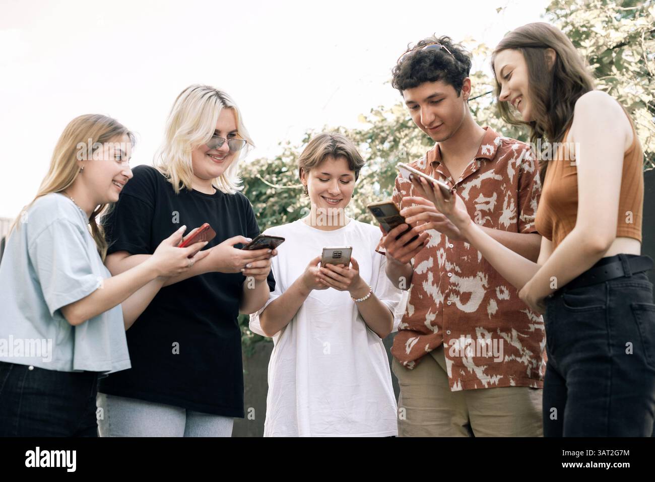 Teenagers smiling while using smartphones outdoors Stock Photo - Alamy