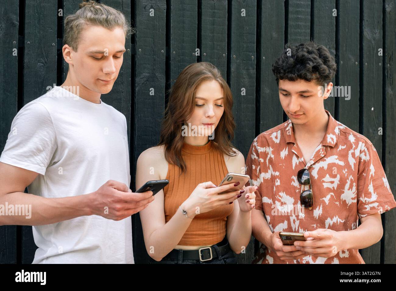 Three young people focused on smartphones outdoors Stock Photo - Alamy