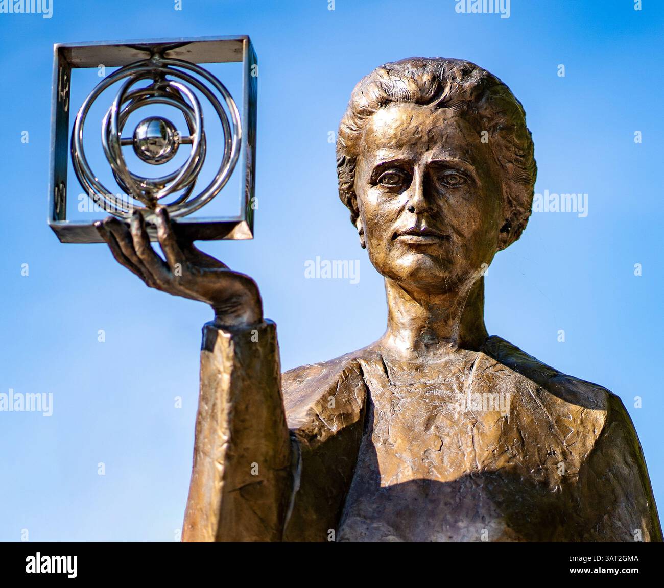 A bronze statue of Marie Curie holding a metallic cube, symbolizing ...