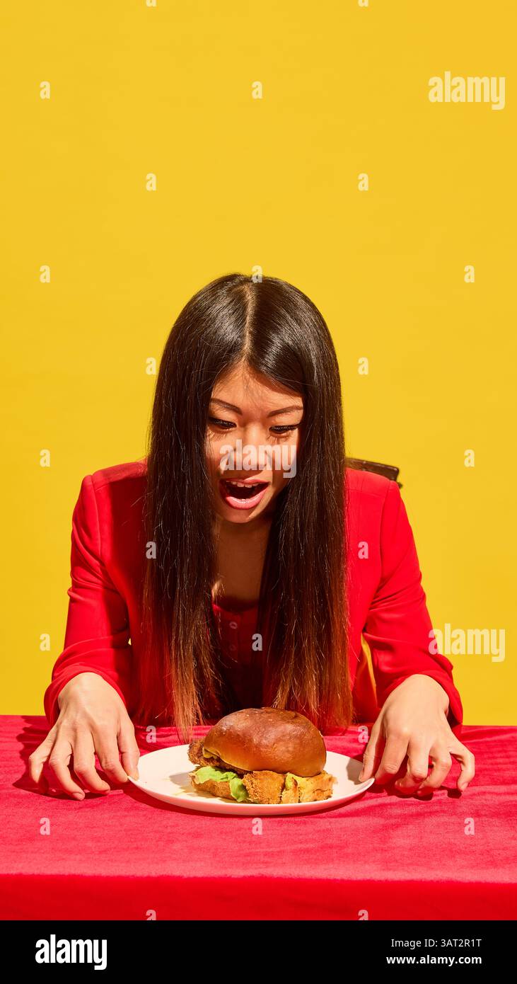 Young woman in red outfit leans over burger with hungry gaze on red ...